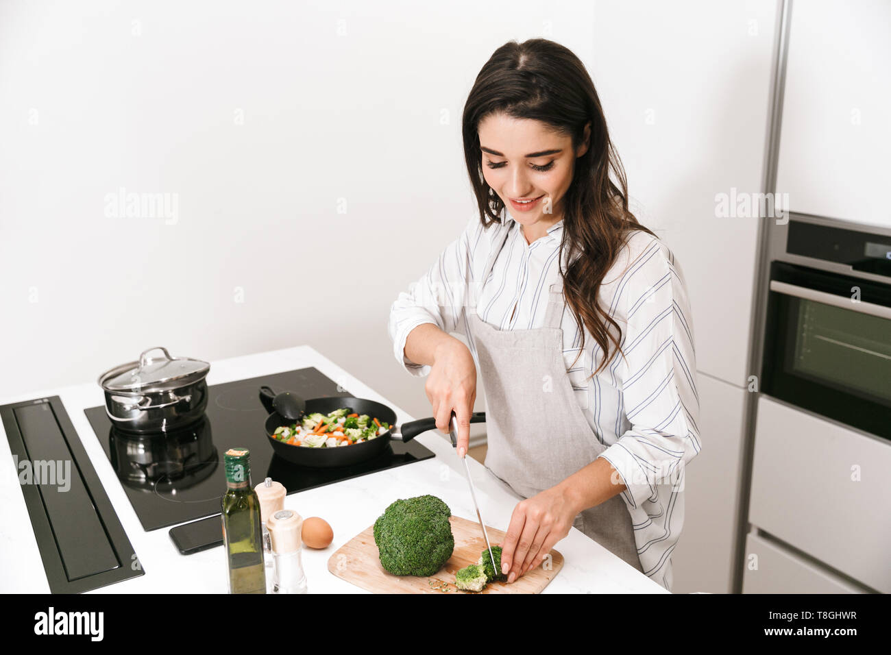 Beautiful young woman cooking healthy dinner at the kitchen, using frying pan Stock Photo - Alamy