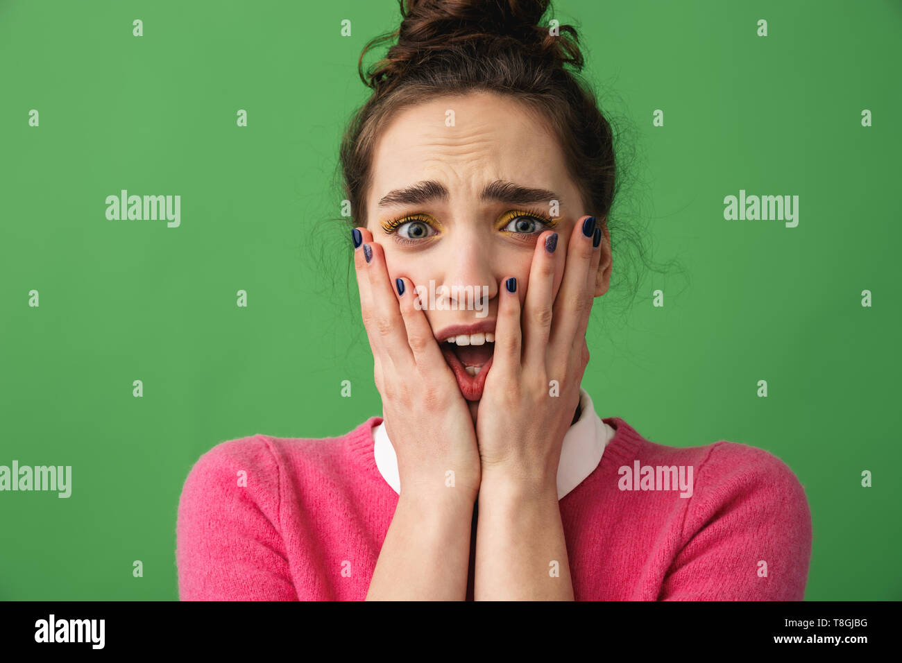 Portrait of a shocked young woman standing isolated over green ...