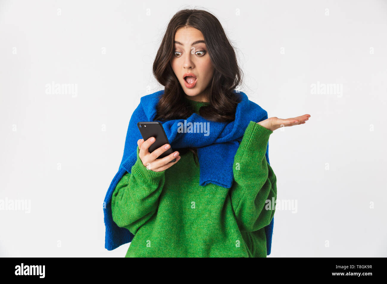 Portrait of perplexed woman 30s with dark hair in casual clothes using mobile phone isolated ...