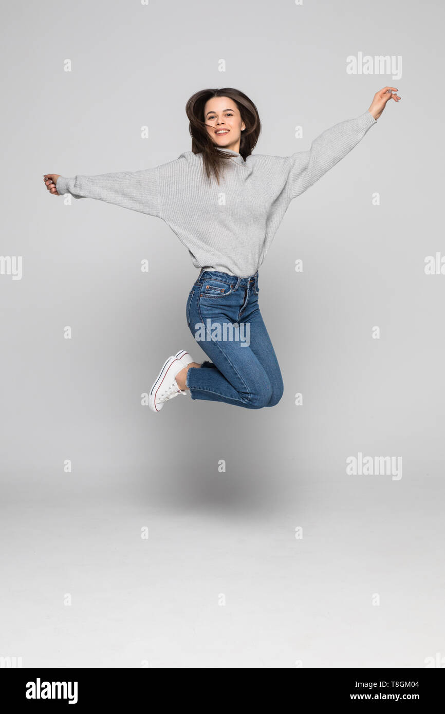 Full length portrait of a laughing woman jumping over gray background ...