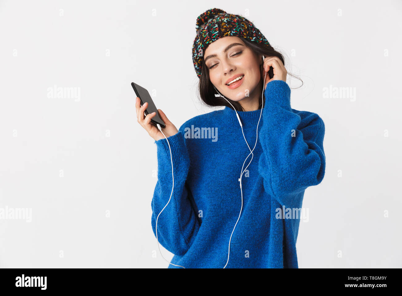 Portrait of ecstatic woman 30s wearing winter hat and earphones holding ...