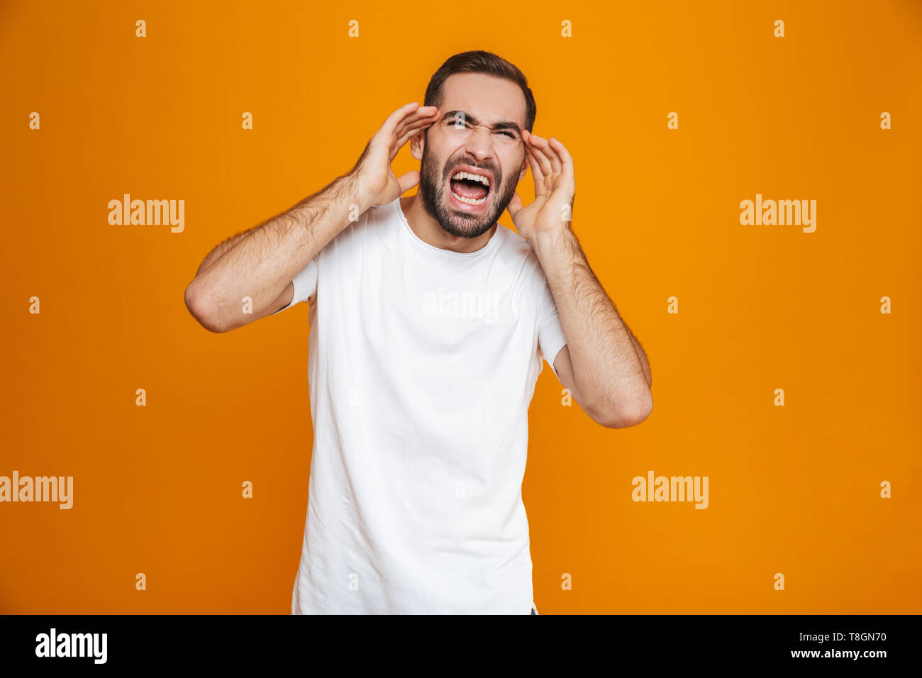 Image of tense guy 30s in t-shirt screaming and rubbing temples because of headache while ...