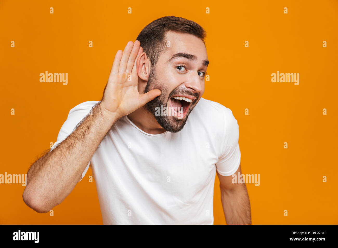 Image of joyful man 30s trying to hear something while keeping hand at ...