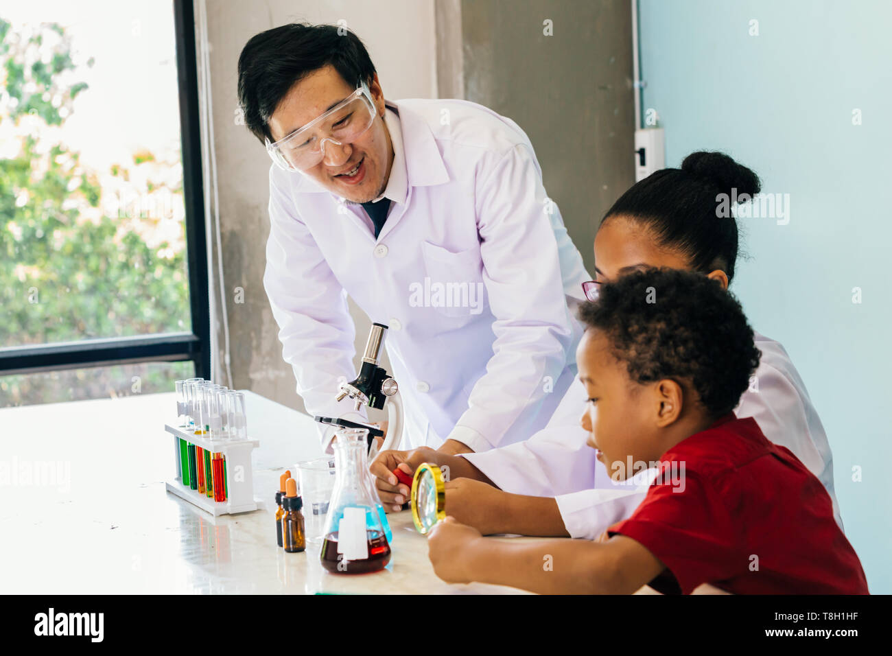 Young Asian scientist holding glass tube flask and teaching two African ...