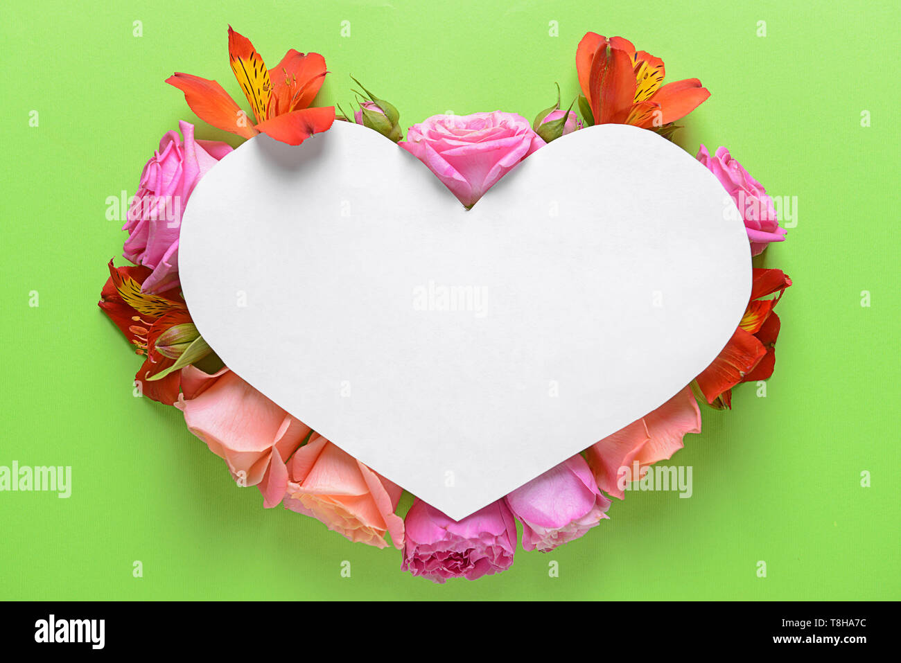 Heart shaped sheet of paper with beautiful flowers on color background ...