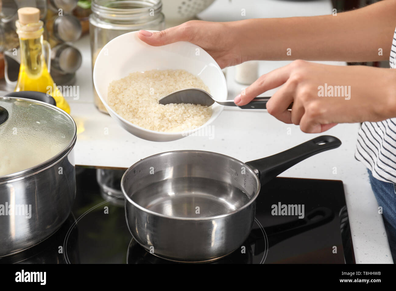 Woman pouring raw rice into saucepan with boiling water on stove Stock ...