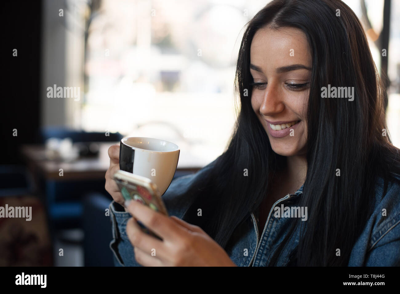 Woman enjoying a cup of tea while using her mobile phone Stock Photo ...