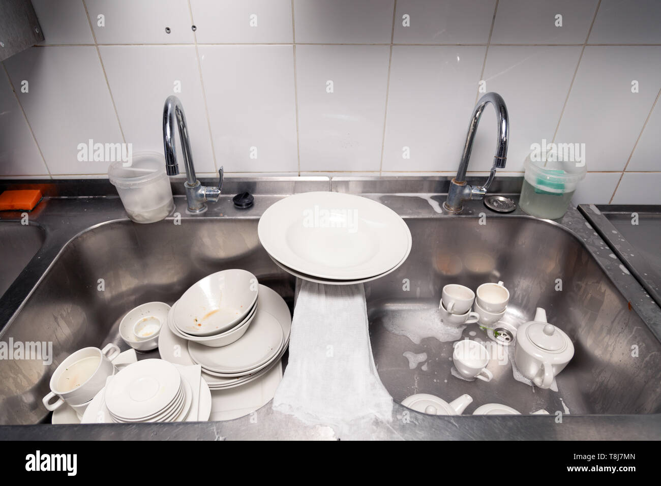 Closeup stack of dirty dishes at bottom of metal square sink at ...