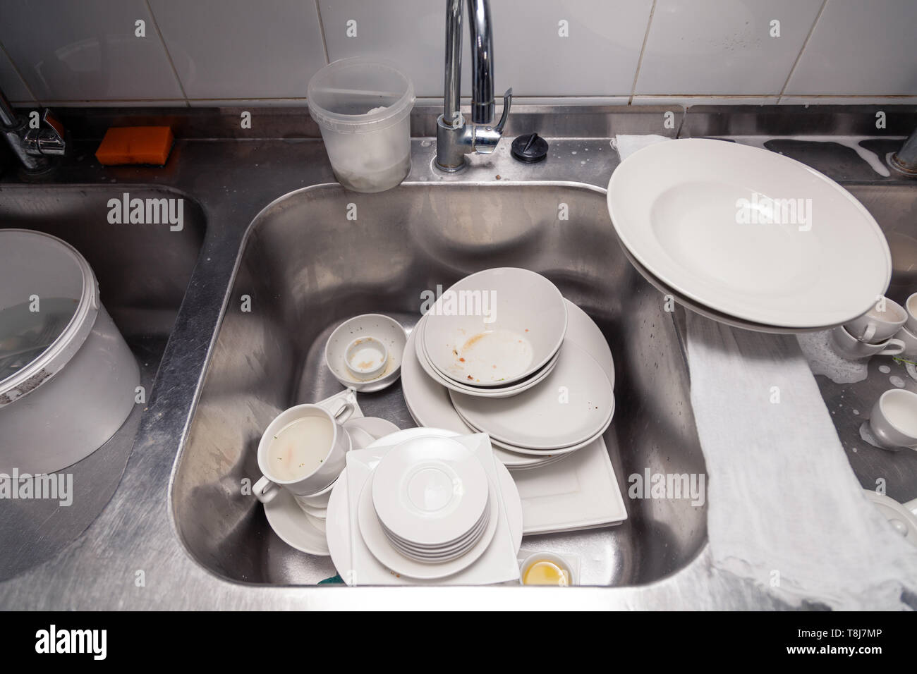 Closeup stack of dirty dishes at bottom of metal square sink at ...