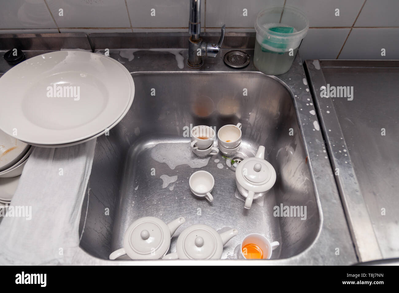 Closeup stack of dirty dishes at bottom of metal square sink at ...
