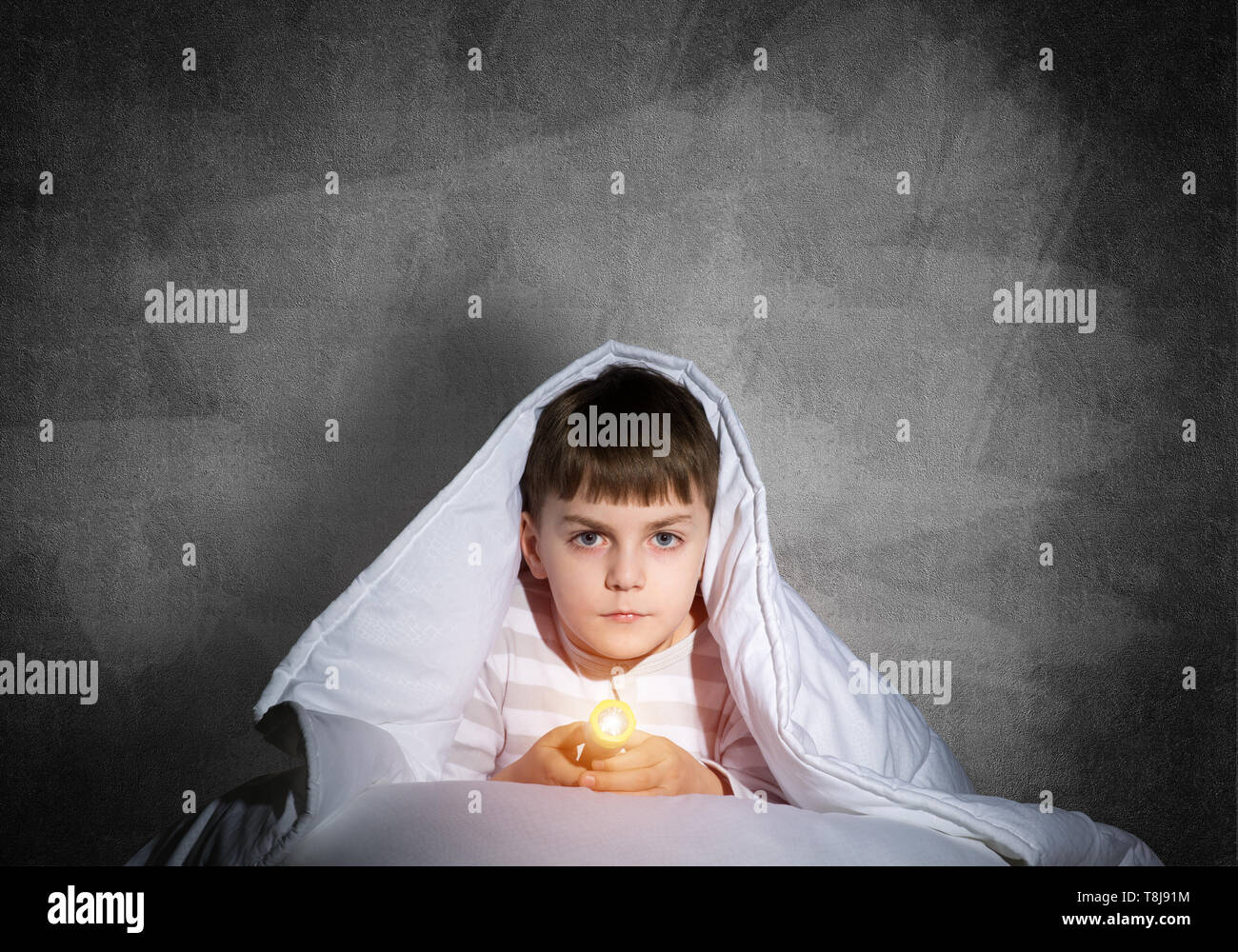 Serious child with flashlight hiding under blanket Stock Photo - Alamy