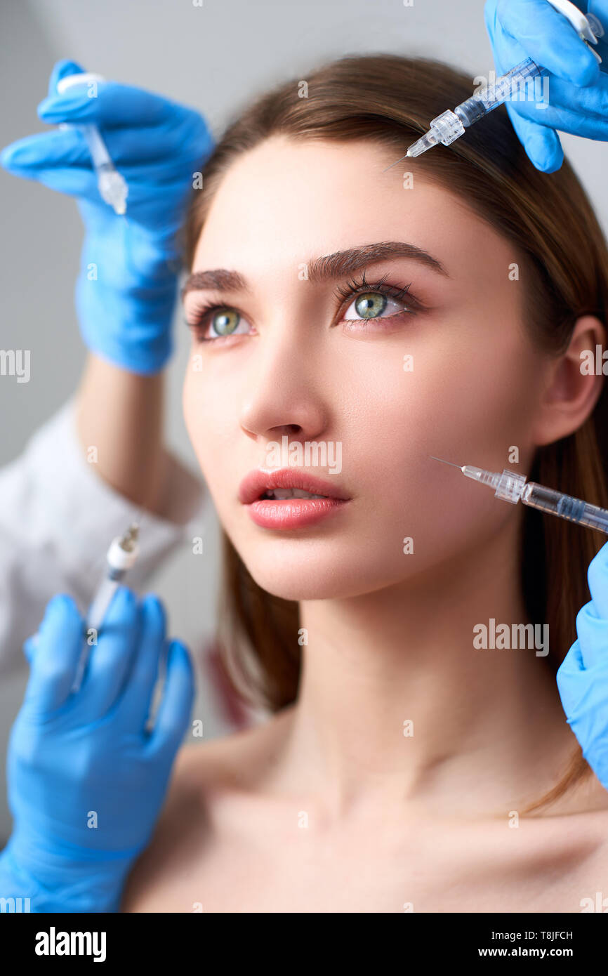 Hands of beauticians holding syringes around doll like woman face ready ...