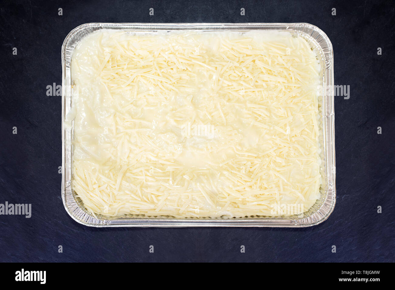 Pre-cooked cold lasagne foil tray. Isolated over black slate board ...