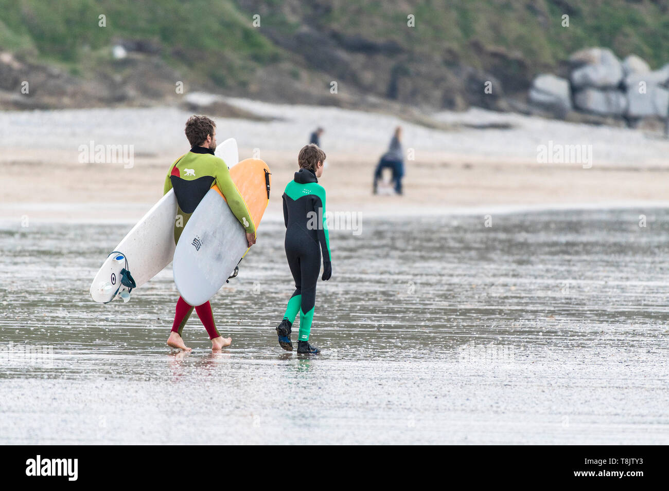 A father and his son carrying their surfboards and walking across the ...