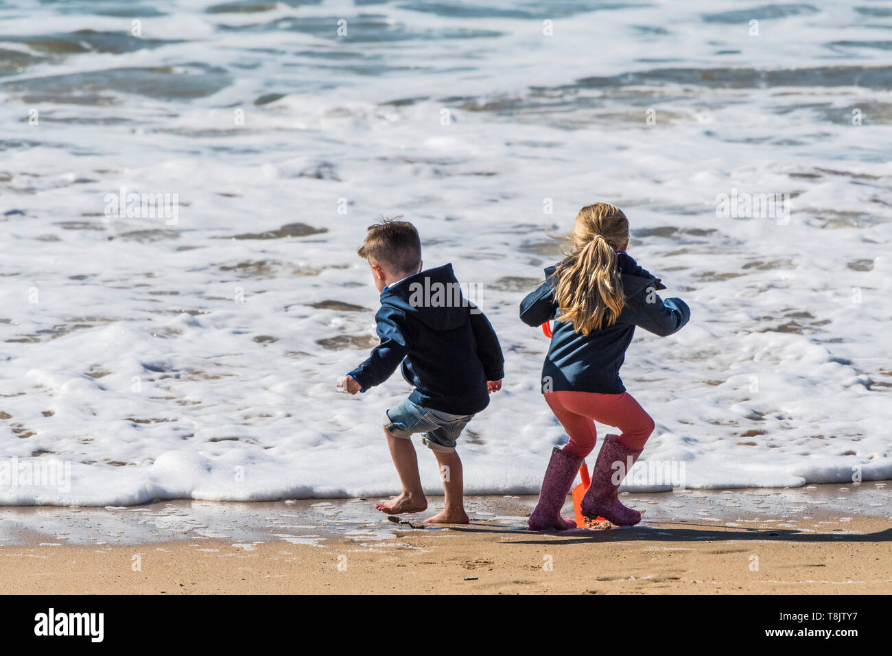 Two young children having fun playing on the shoreline on Fistral Beach ...