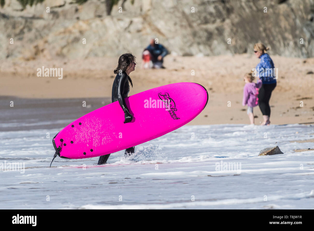 A tired female surfer carrying a colourful surfboard and walking out of ...