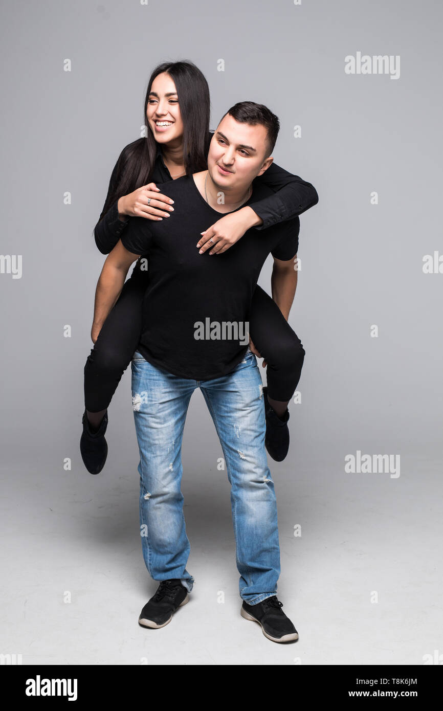 Young couple having fun riding piggy back laughing on grey background ...