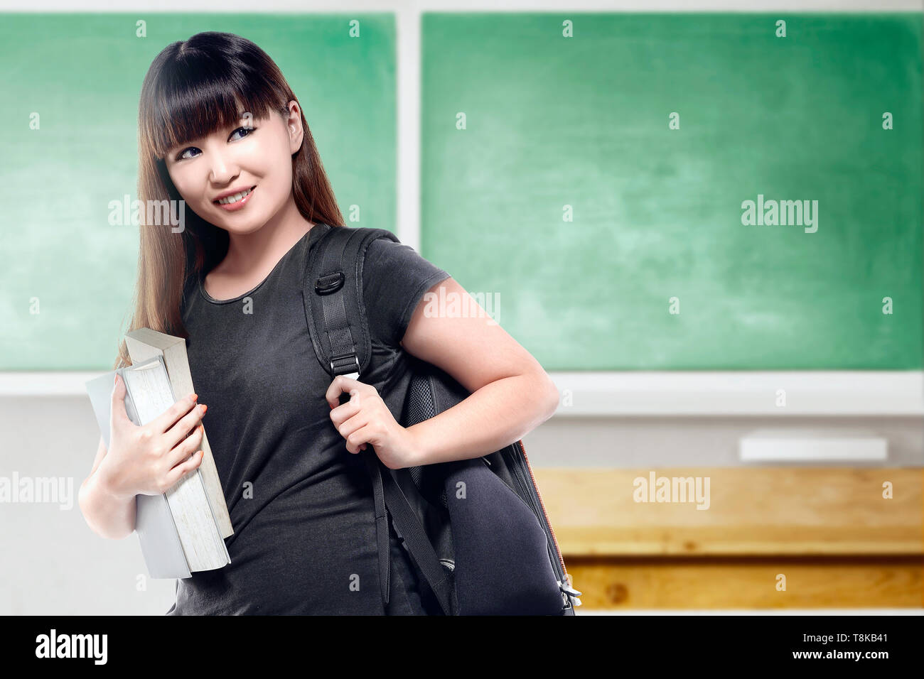 Asian student woman with backpack carrying book in the classroom with ...