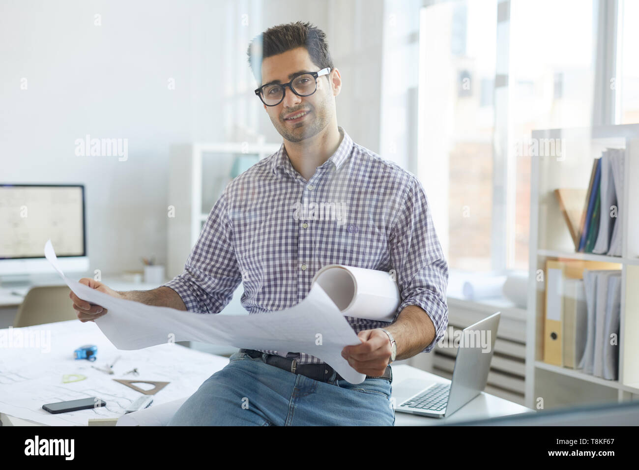 Smiling Engineer Holding Plans at Workplace Stock Photo - Alamy