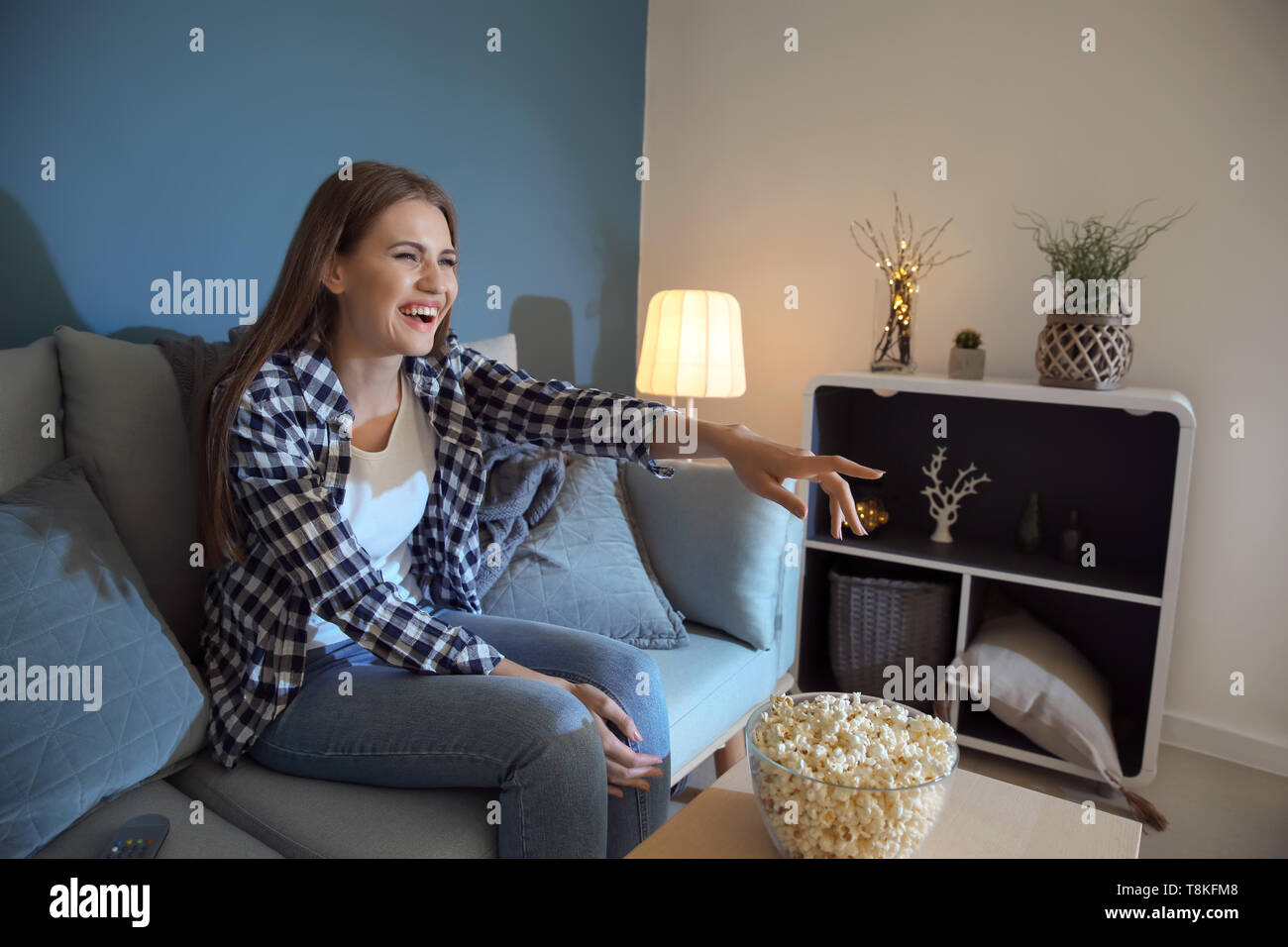 Emotional young woman eating popcorn while watching TV late in evening ...