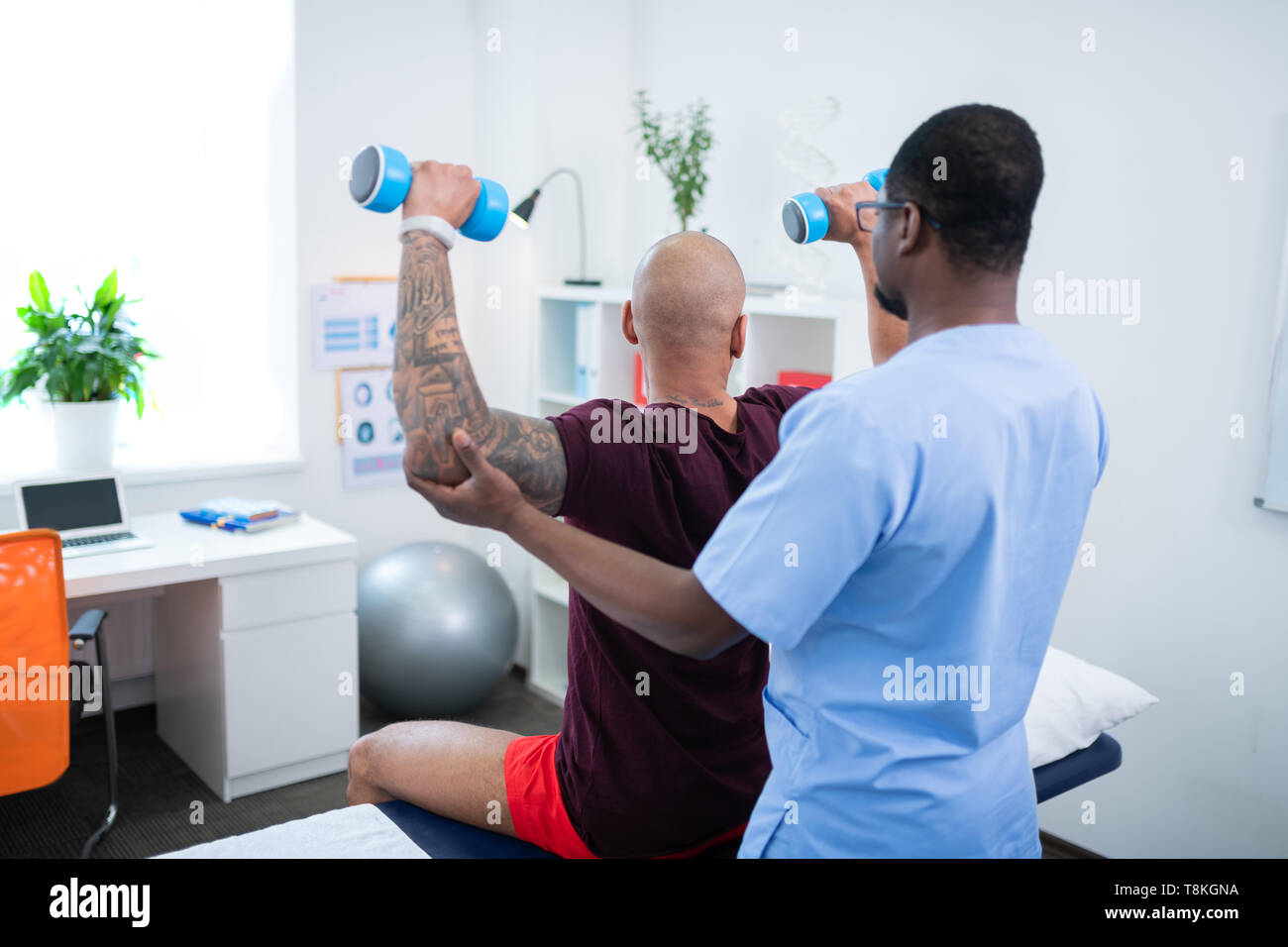 Therapist helping his patient doing exercises with barbells Stock Photo ...