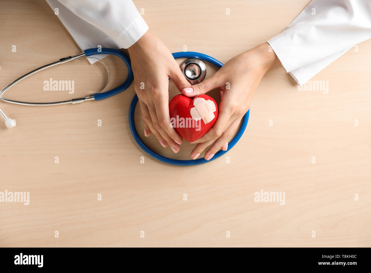 Hands of cardiologist with medical stethoscope and red heart on light ...