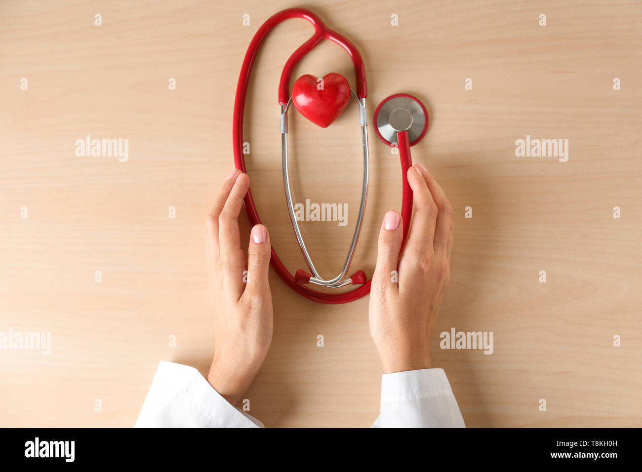Hands of cardiologist with medical stethoscope and red heart on light ...