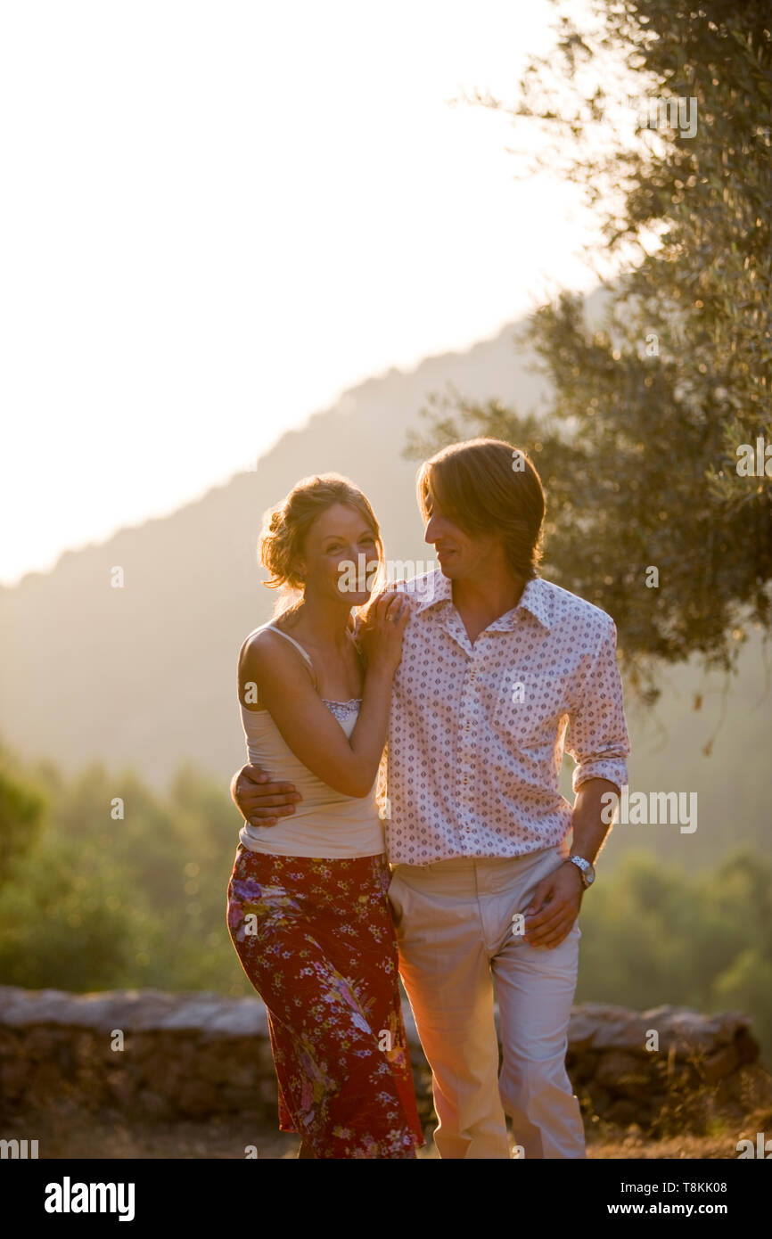 Mid adult couple hugging while walking on a country lane at sunset ...
