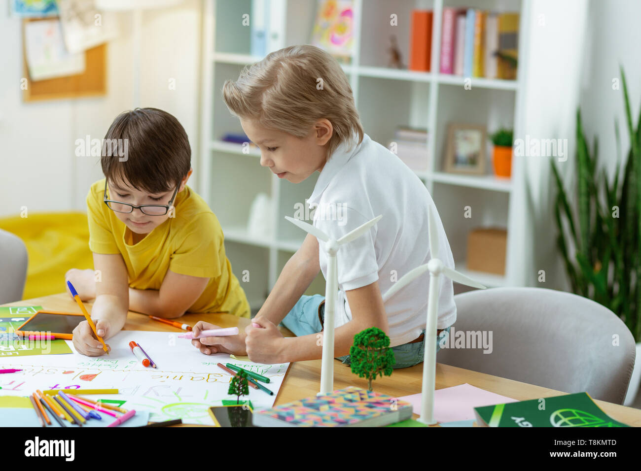 Curious little boys being concentrated on drawing poster with markers ...