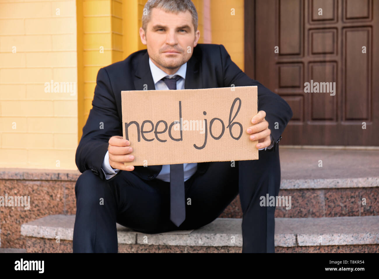 Fired businessman holding piece of cardboard with text NEED JOB while ...