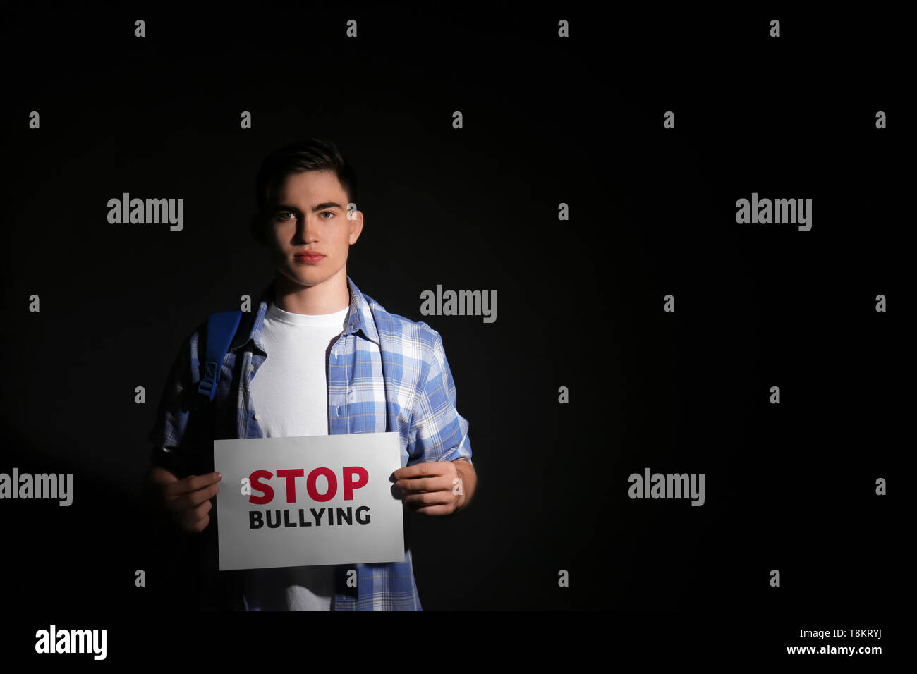 Teenage boy holding sheet of paper with text STOP BULLYING on dark ...