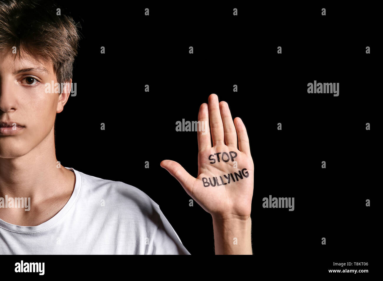Teenage boy with text STOP BULLYING written on hand against dark ...