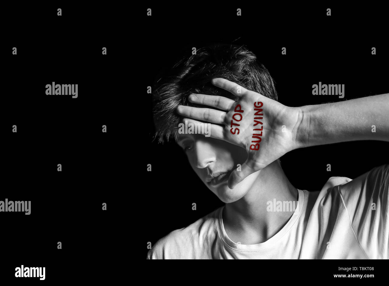 Teenage boy with red text STOP BULLYING written on hand against dark ...
