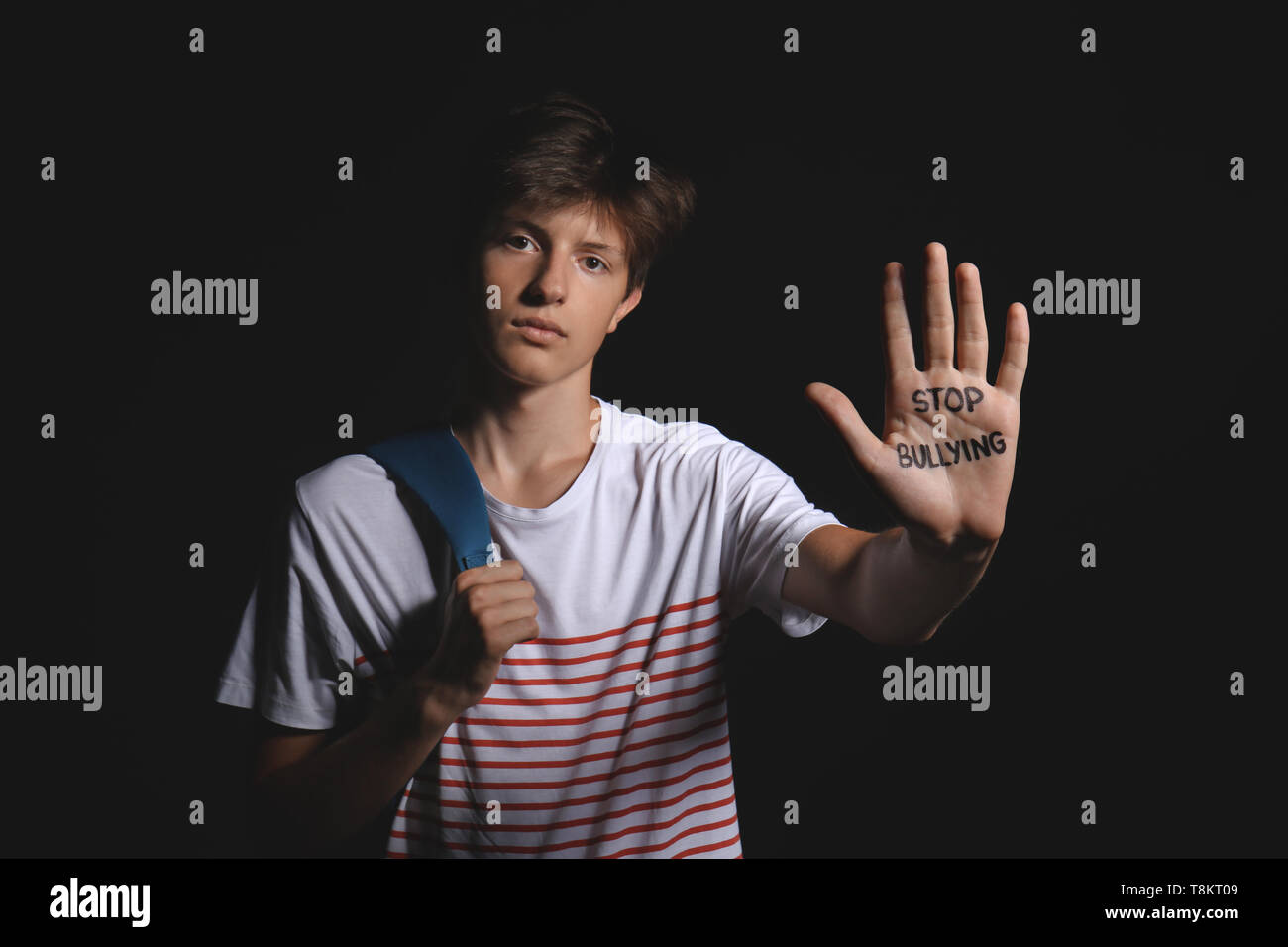 Teenage boy with text STOP BULLYING written on hand against dark ...