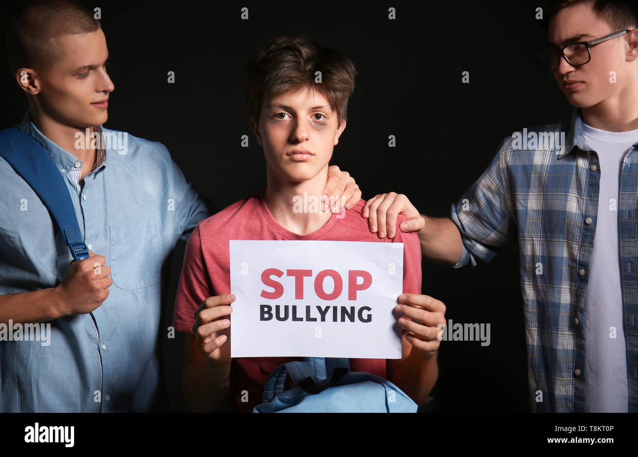 Boy with sheet of paper and aggressive teenagers on dark background ...