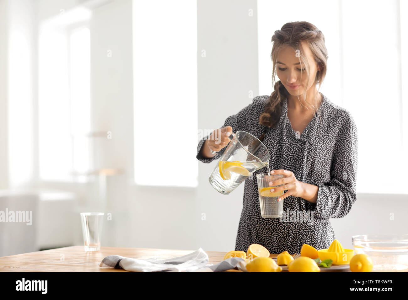 Young woman pouring fresh lemonade from jug into glass at home Stock ...
