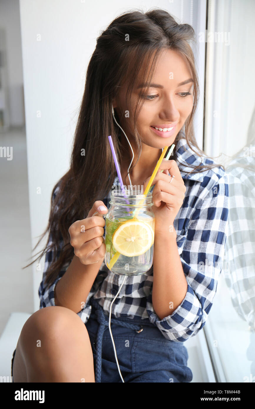 Young woman drinking fresh lemonade while sitting on window sill Stock ...