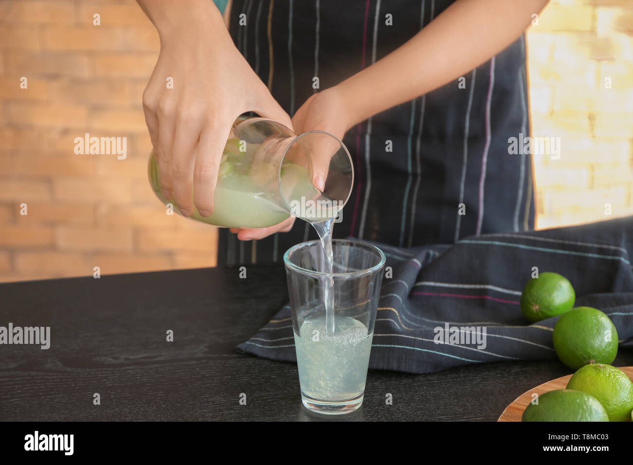Woman pouring fresh lime lemonade from jug into glass Stock Photo - Alamy