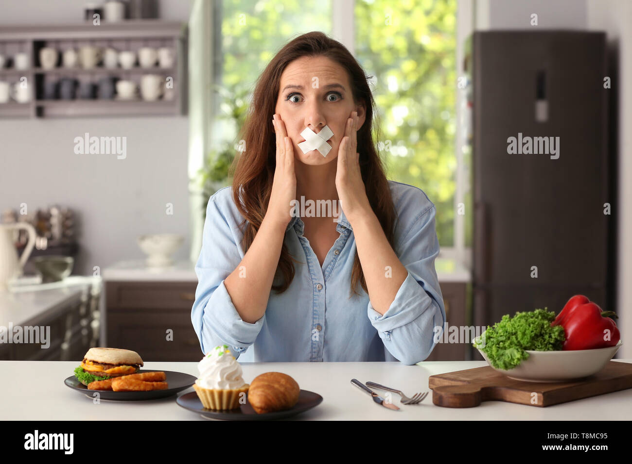 Stressful woman with taped mouth and different products in kitchen ...