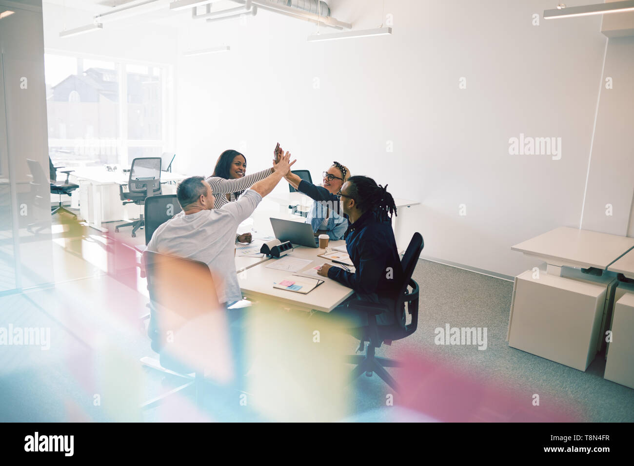 Laughing Group Of Diverse Coworkers High Fiving Together While Sitting