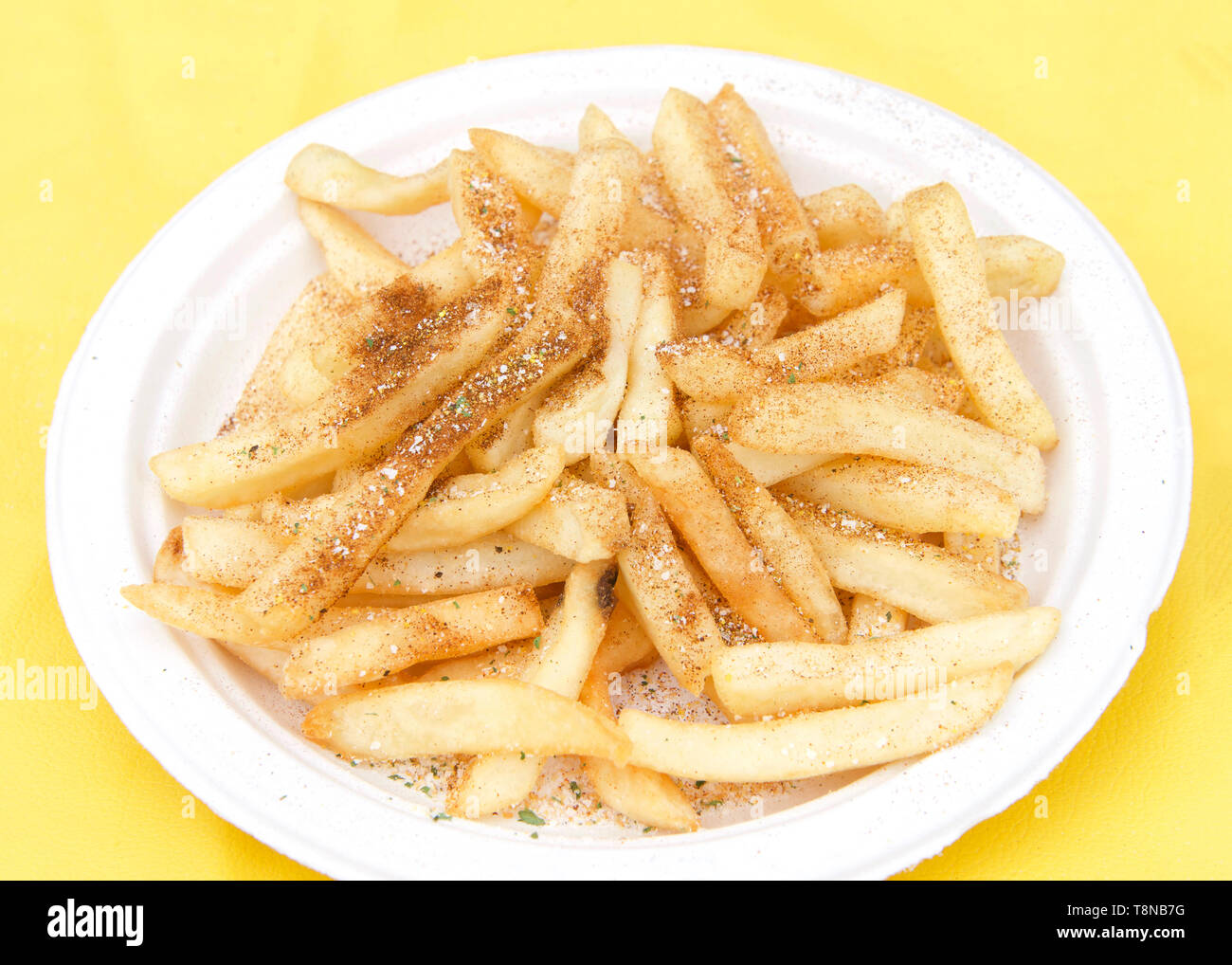 White paper plate with seasoned french fries on yellow table cloth ...