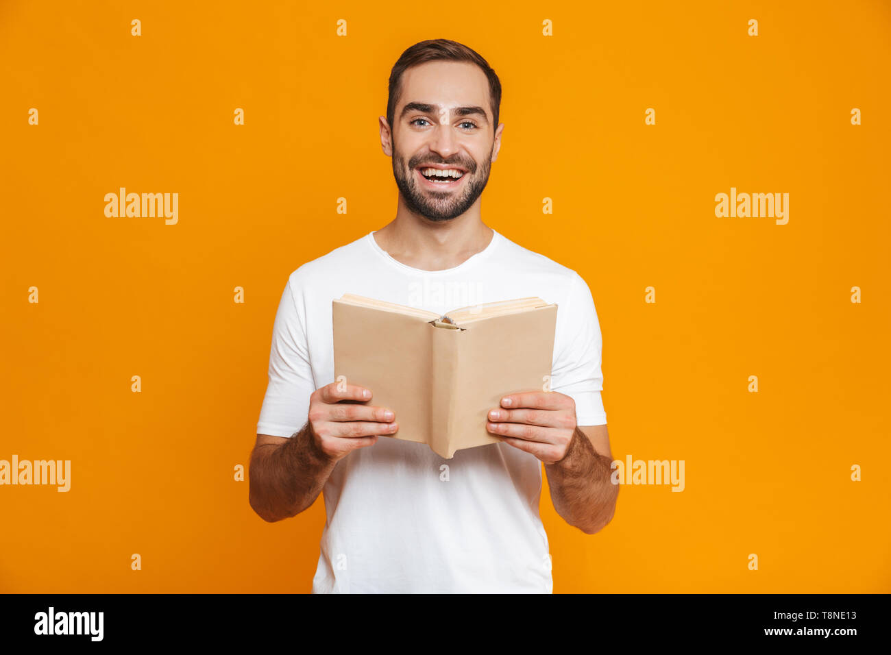 Image of optimistic man 30s in white t-shirt holding and reading book ...