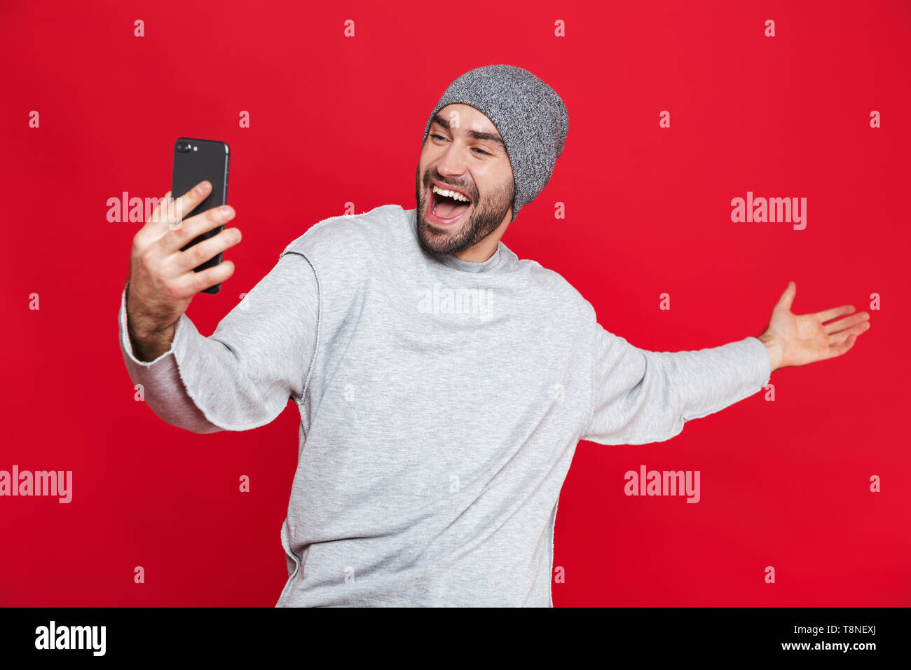 Image of joyous man 30s with beard and mustache holding smartphone ...