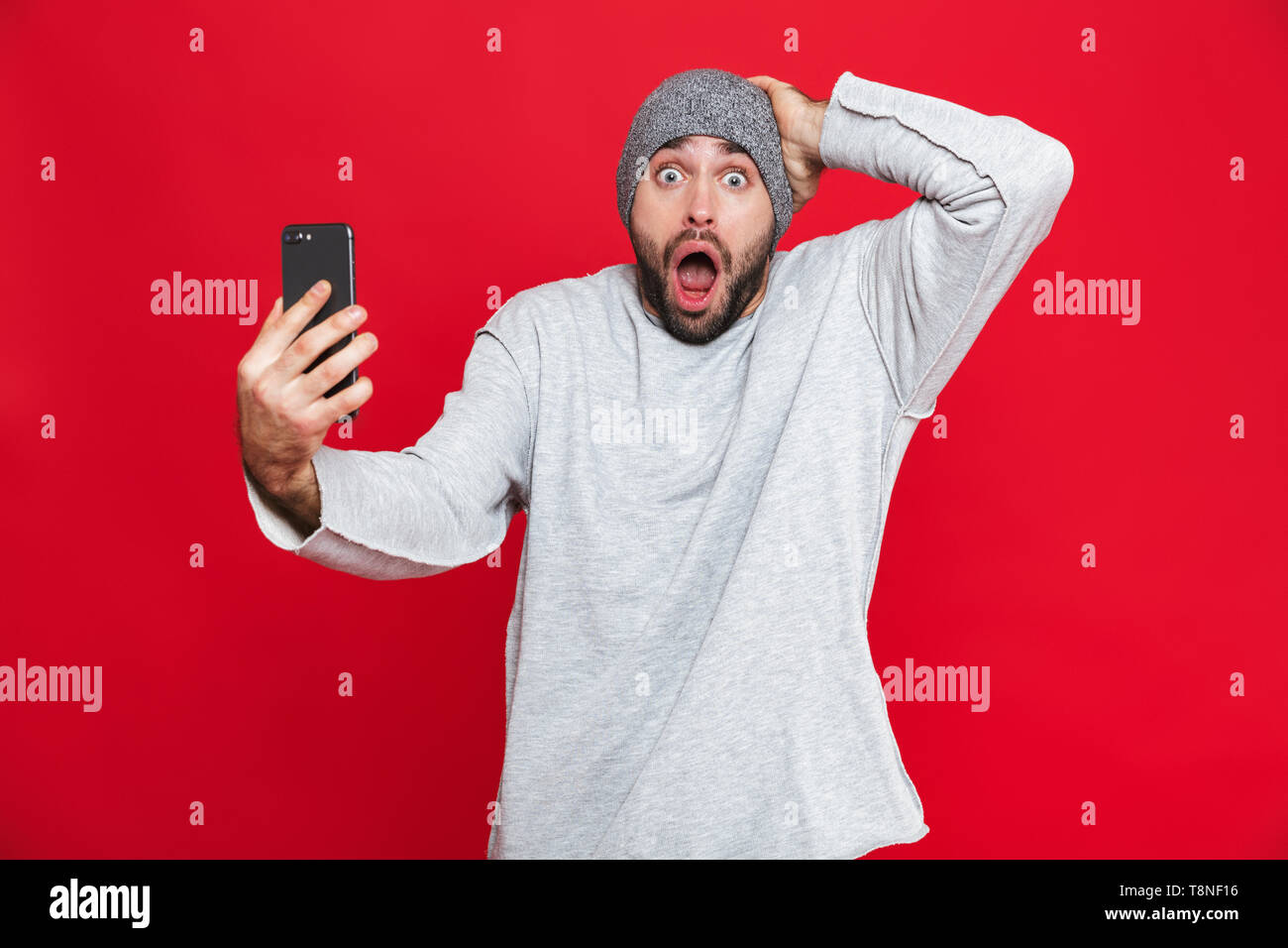 Image of caucasian man 30s grabbing head and holding smartphone while ...