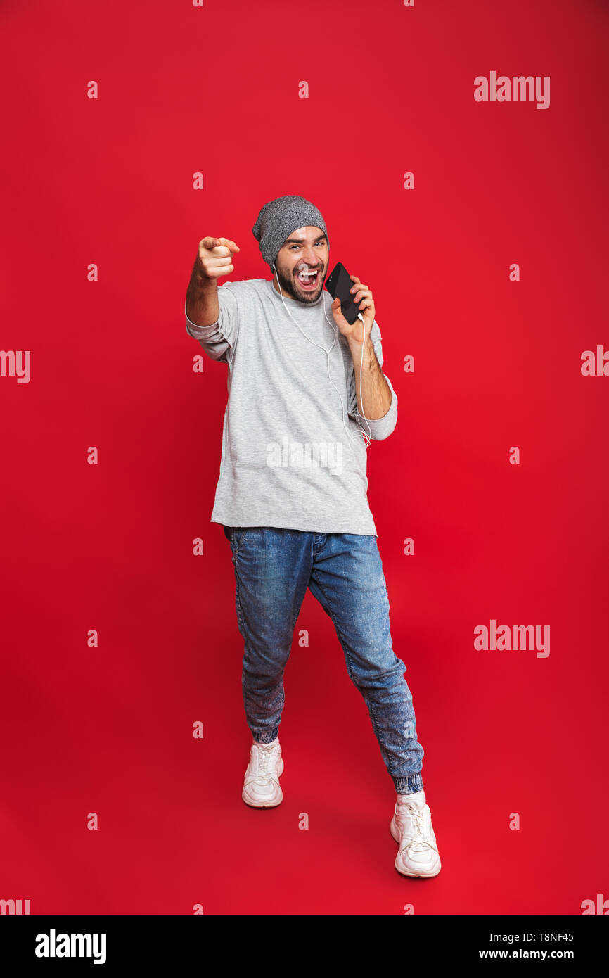 Full length photo of cheerful man 30s singing while listening to music ...