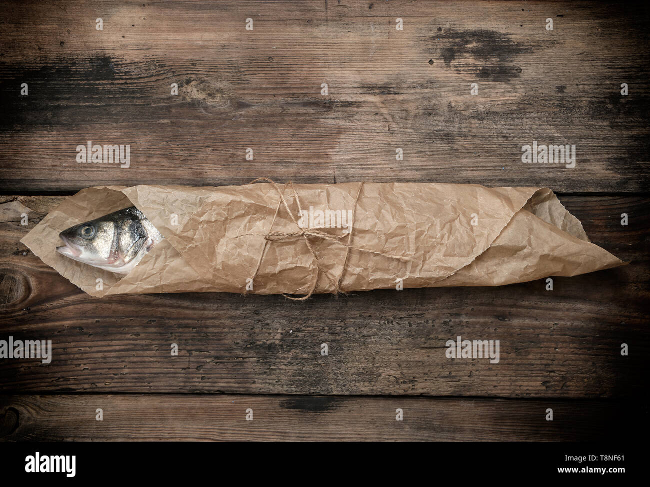 Fresh whole sea bass fish wrapped in a brown paper and tied with a rope ...