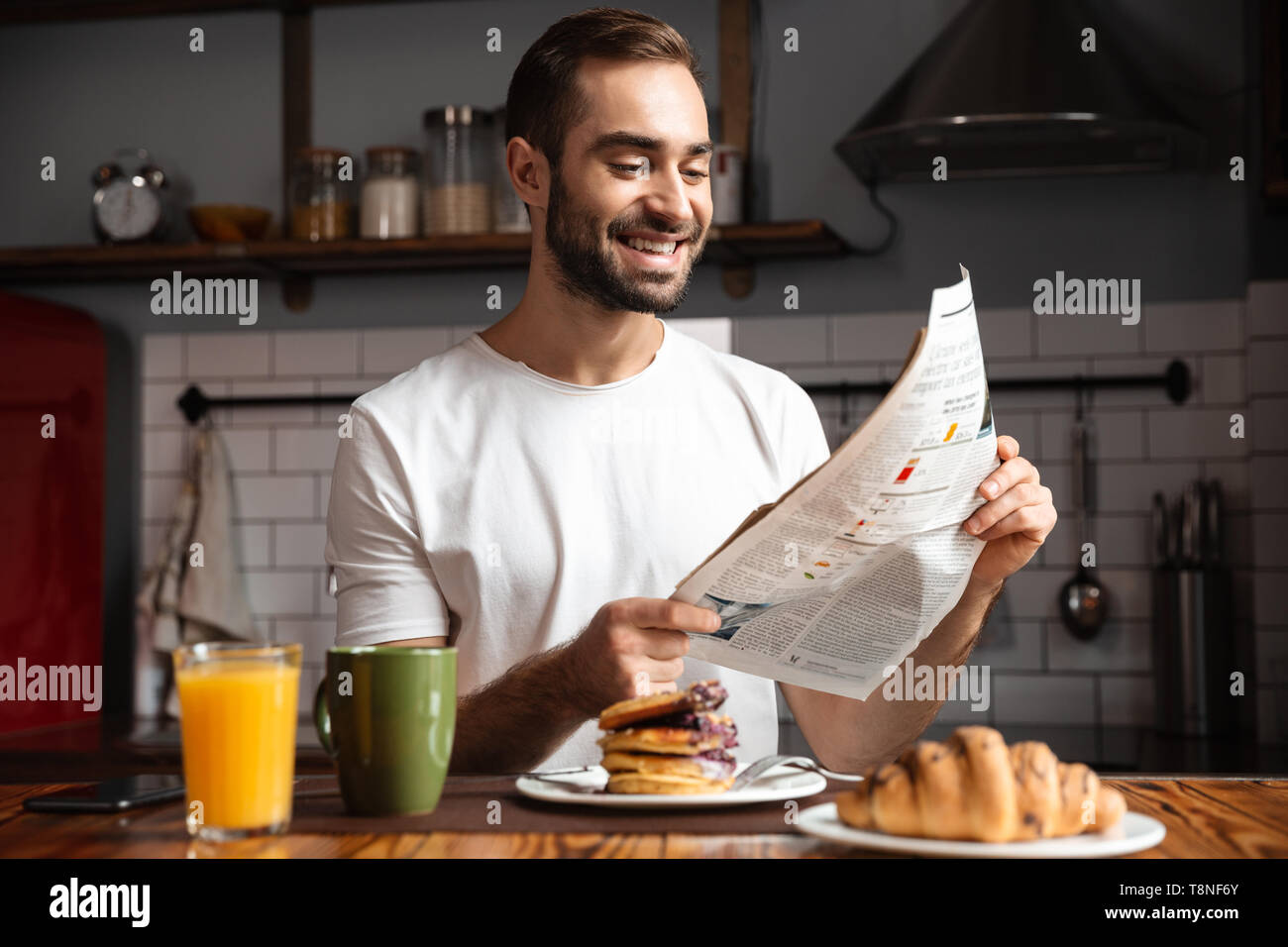 Smiling man having breakfast, reading newspaper Stock Photo - Alamy