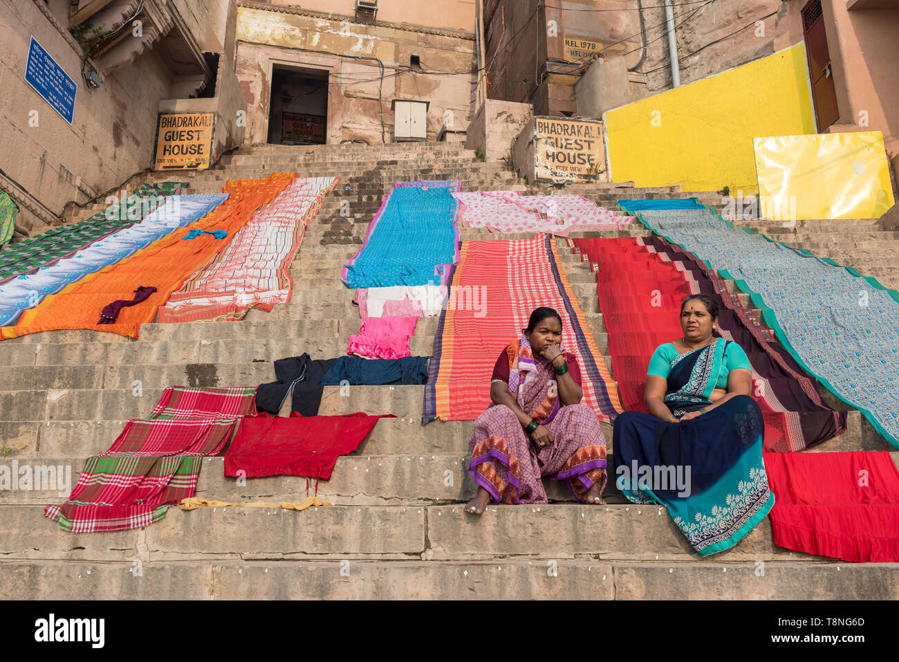 Two women and coulourful fabrics drying in the sun on steps (ghats) of ...