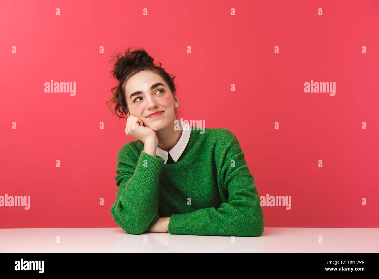 Pretty nerd girl sitting at the table isolated over pink background ...