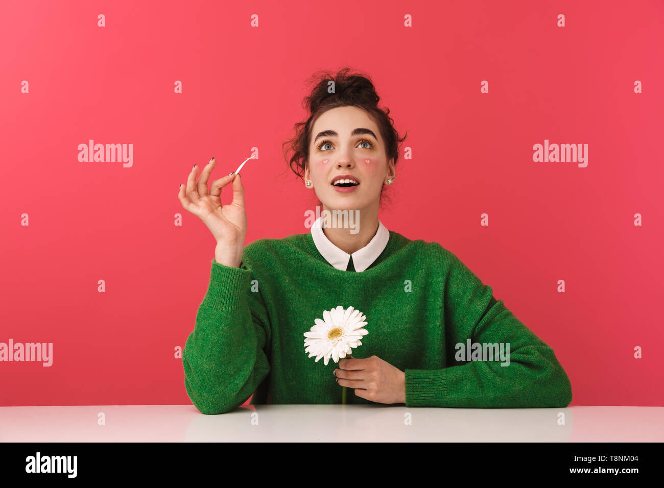 Pretty nerd girl sitting at the table isolated over pink background ...